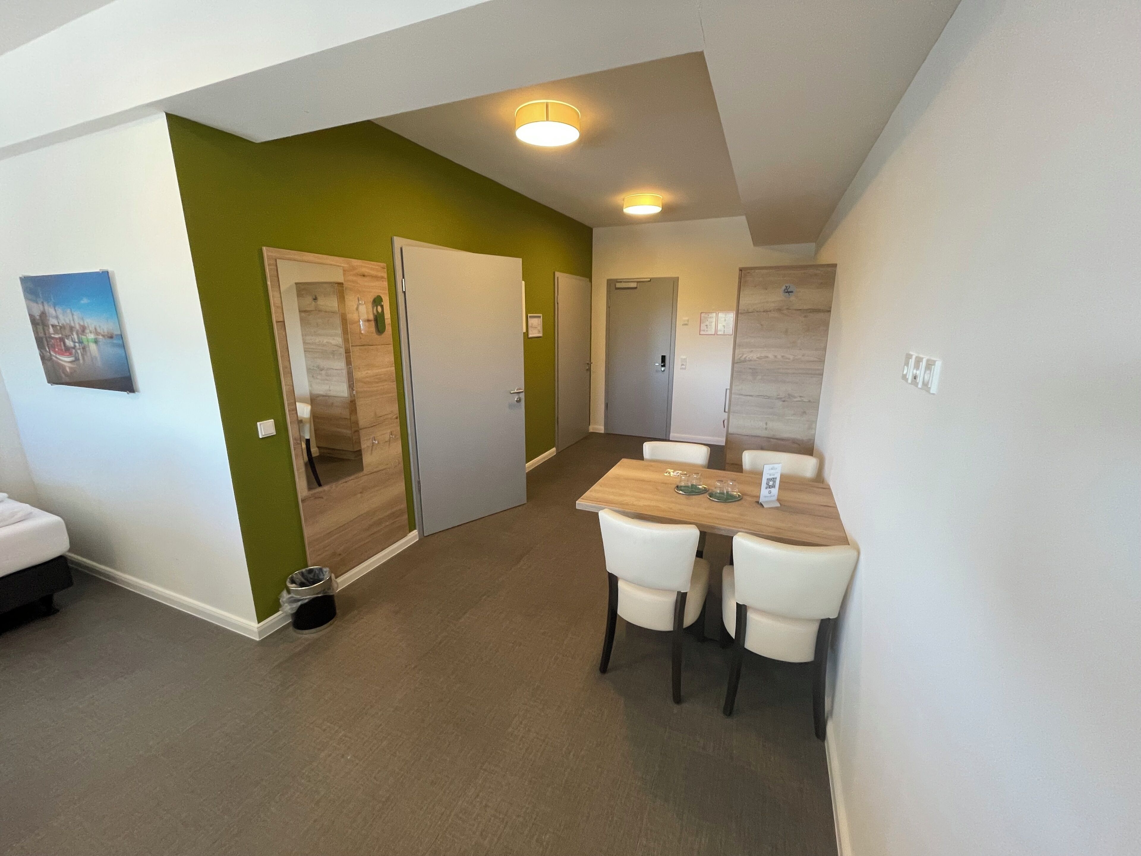 Quarto de hotel moderno com área de refeições, banheiro com chuveiro e corredor que leva a outro quarto.