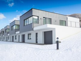 Um edifício residencial moderno, de vários andares, com amplas janelas e telhado plano, localizado numa encosta coberta de neve.