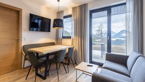 Uma sala de estar moderna com uma mesa de jantar de madeira, sofá cinza e TV fixada na parede.