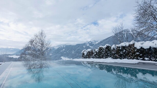Uma piscina infinita com vista clara para montanhas cobertas de neve e um lago.