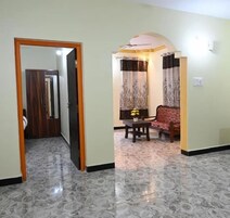 Um quarto com piso de mármore, porta de madeira, sofá e cortinas.