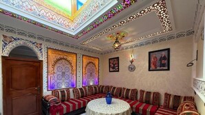 Quarto com decoração tradicional, apresentando um conjunto de sofás, uma mesa redonda e detalhes decorativos no teto.