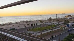 Uma área urbana costeira com edifícios, uma estrada e vista para o mar ao pôr do sol.