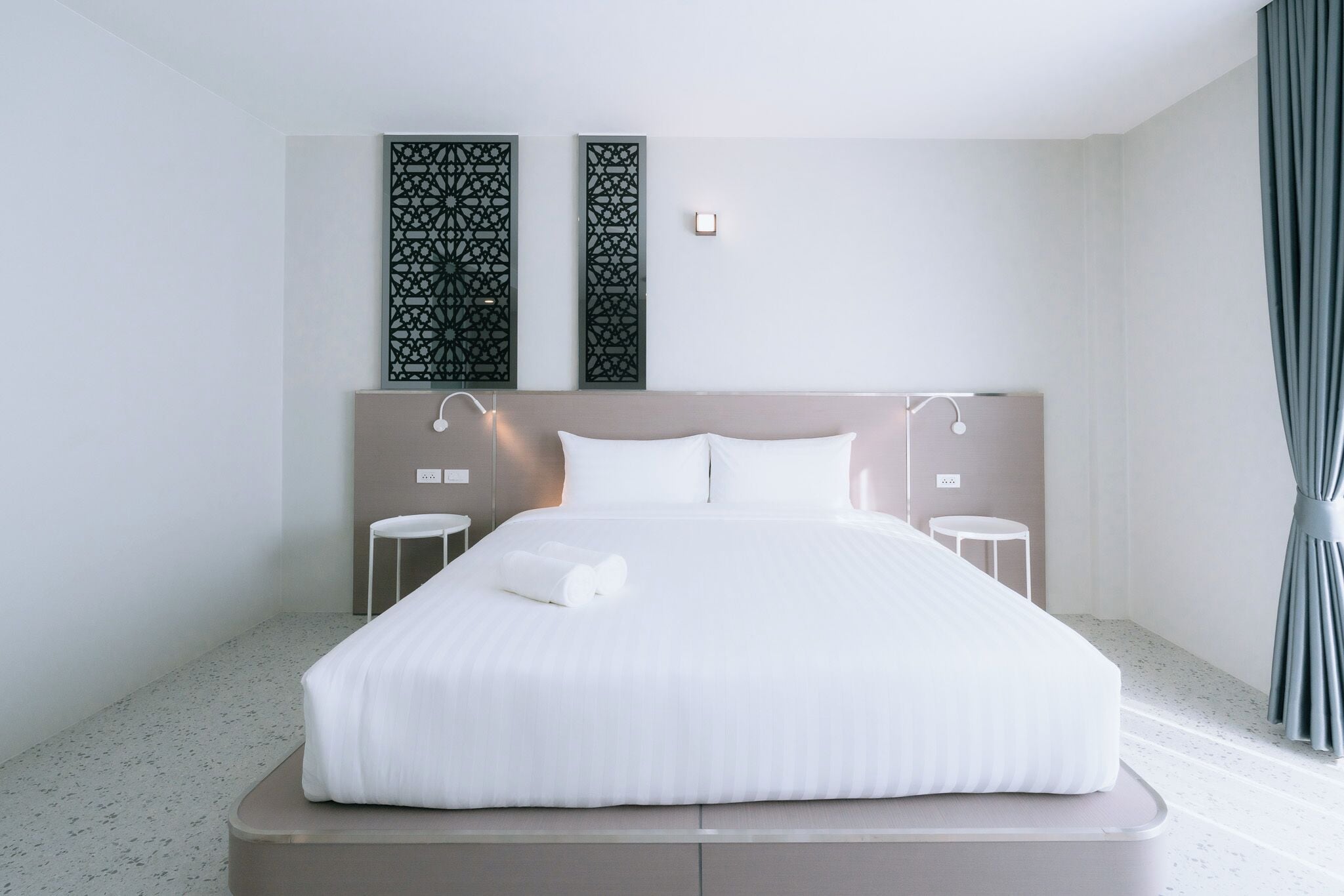 Quarto de hotel moderno com uma cama grande, duas luminárias fixadas na parede e um painel decorativo sobre a cama.