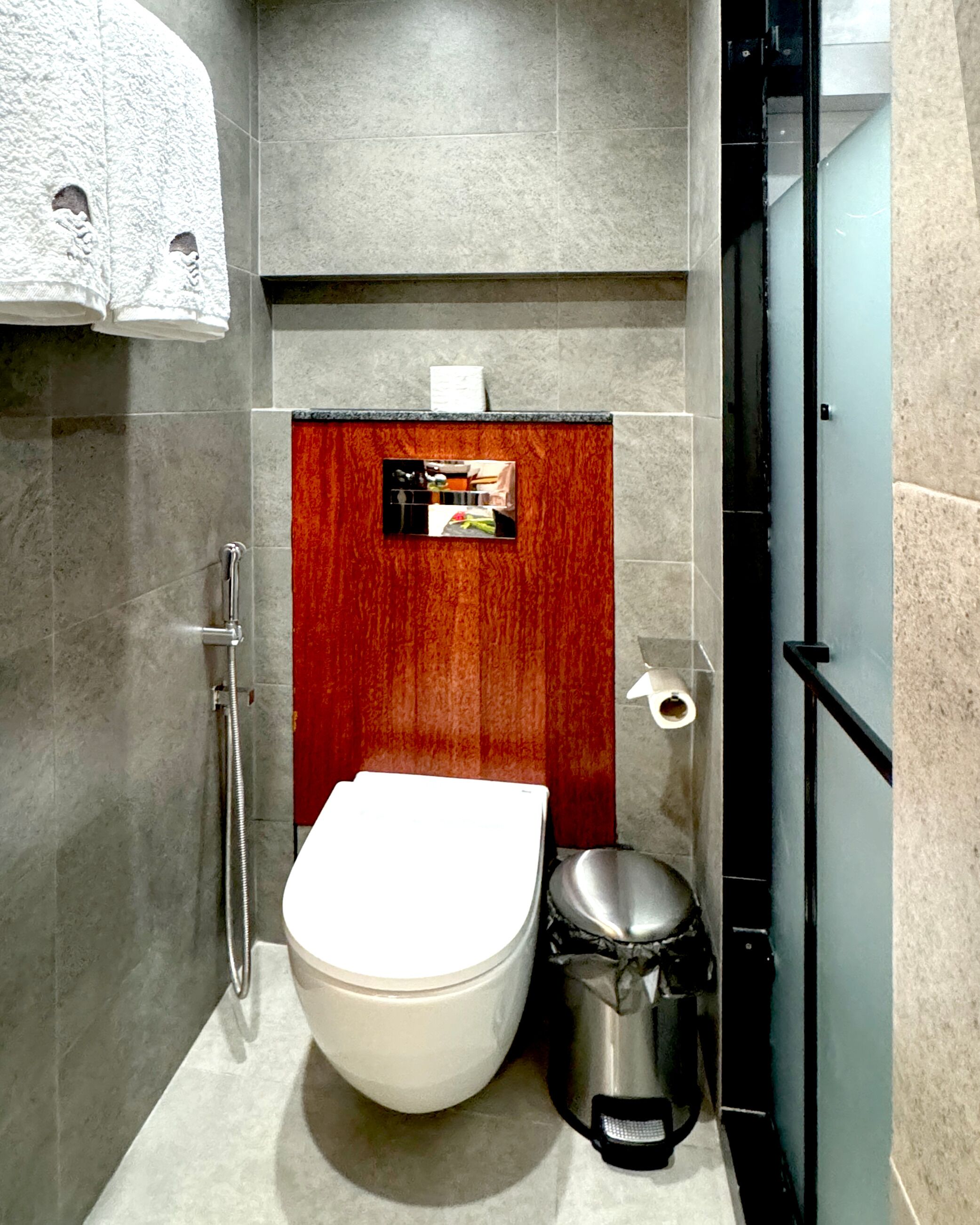 Uma casa de banho moderna com sanita branca, um contentor de lixo em aço inoxidável e zona de duche.