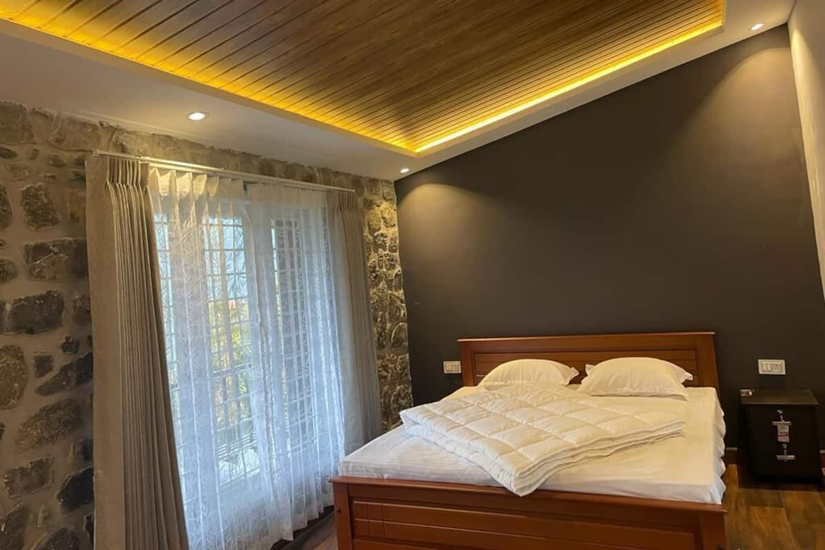 Quarto com parede de pedra, teto de madeira e cama com roupa de cama branca.