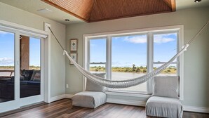Quarto com rede, dois espaços de estar acolchoados, janelas amplas e vista para o exterior.