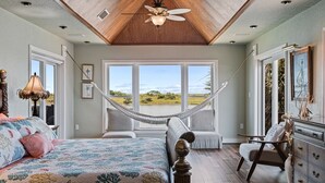 Quarto com uma cama grande, uma rede, vista para o exterior e um ventilador de teto.