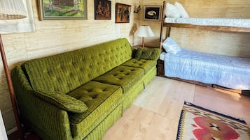 Um quarto com sofá verde, beliche, luminária e obras de arte nas paredes.