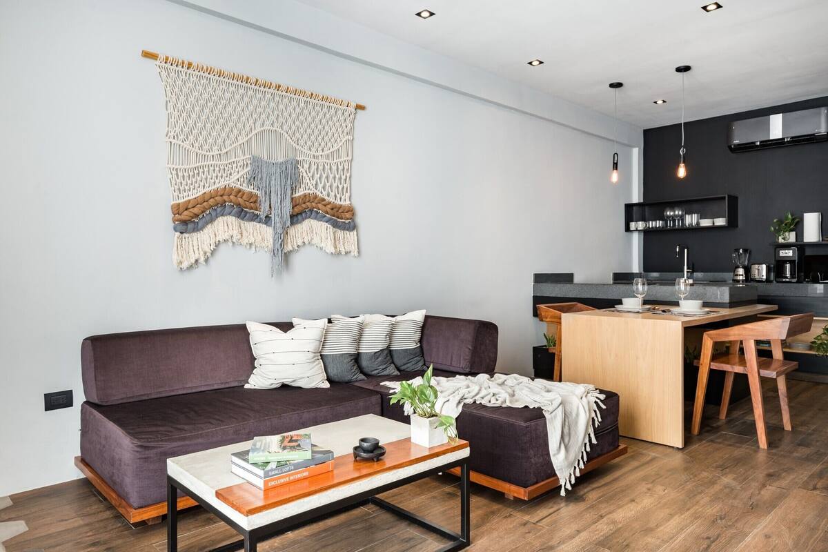Uma sala de estar moderna com um sofá marrom escuro, uma mesa de centro de madeira e um painel de parede em macramé.