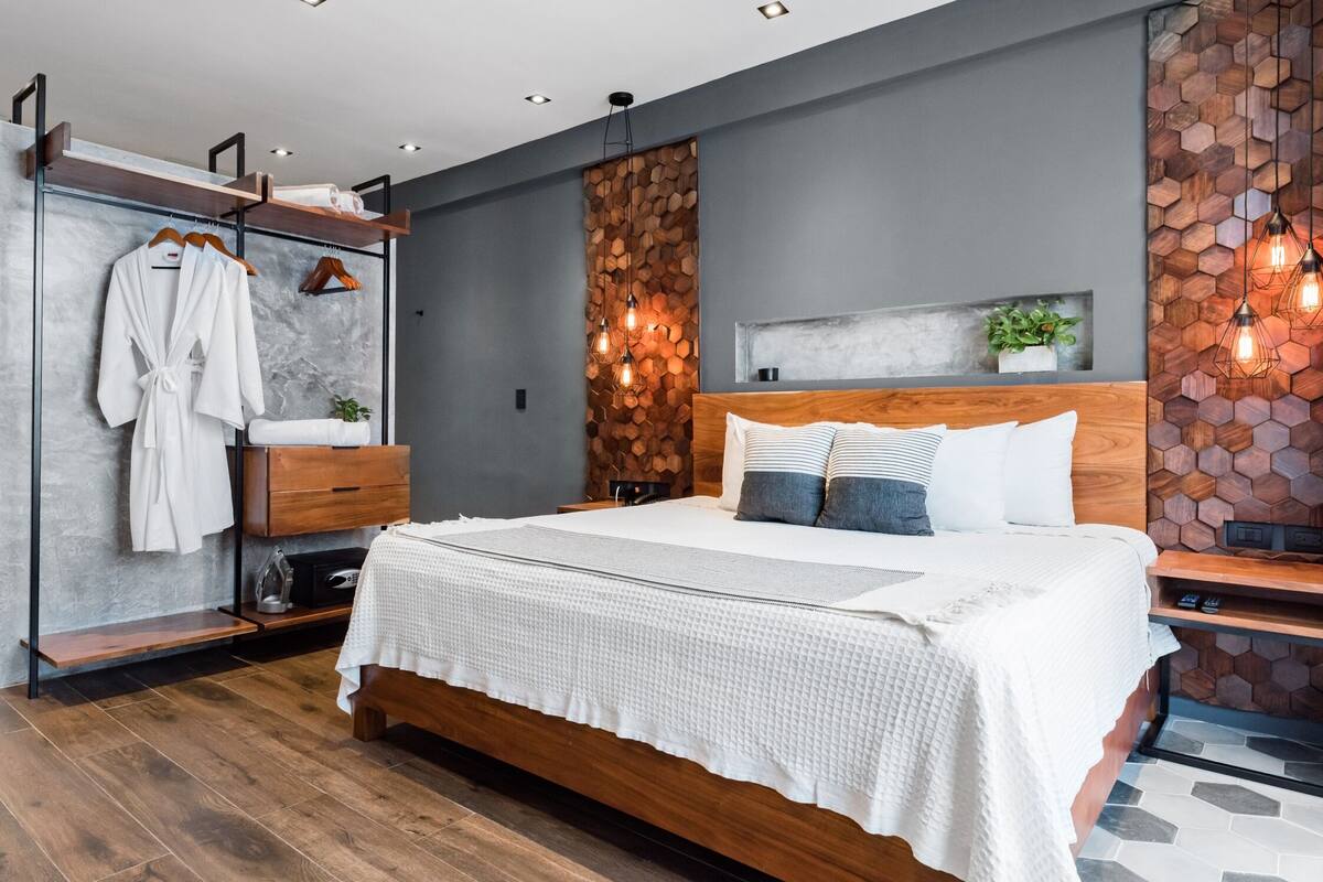 Quarto moderno com cama grande, cabeceira de madeira e roupeiro embutido com espelho.