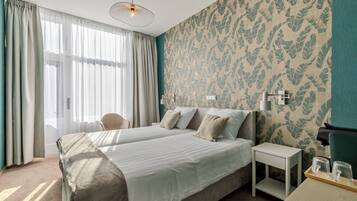 Quarto de hotel com uma cama grande, duas mesas de cabeceira, uma cadeira e uma janela com cortinas.