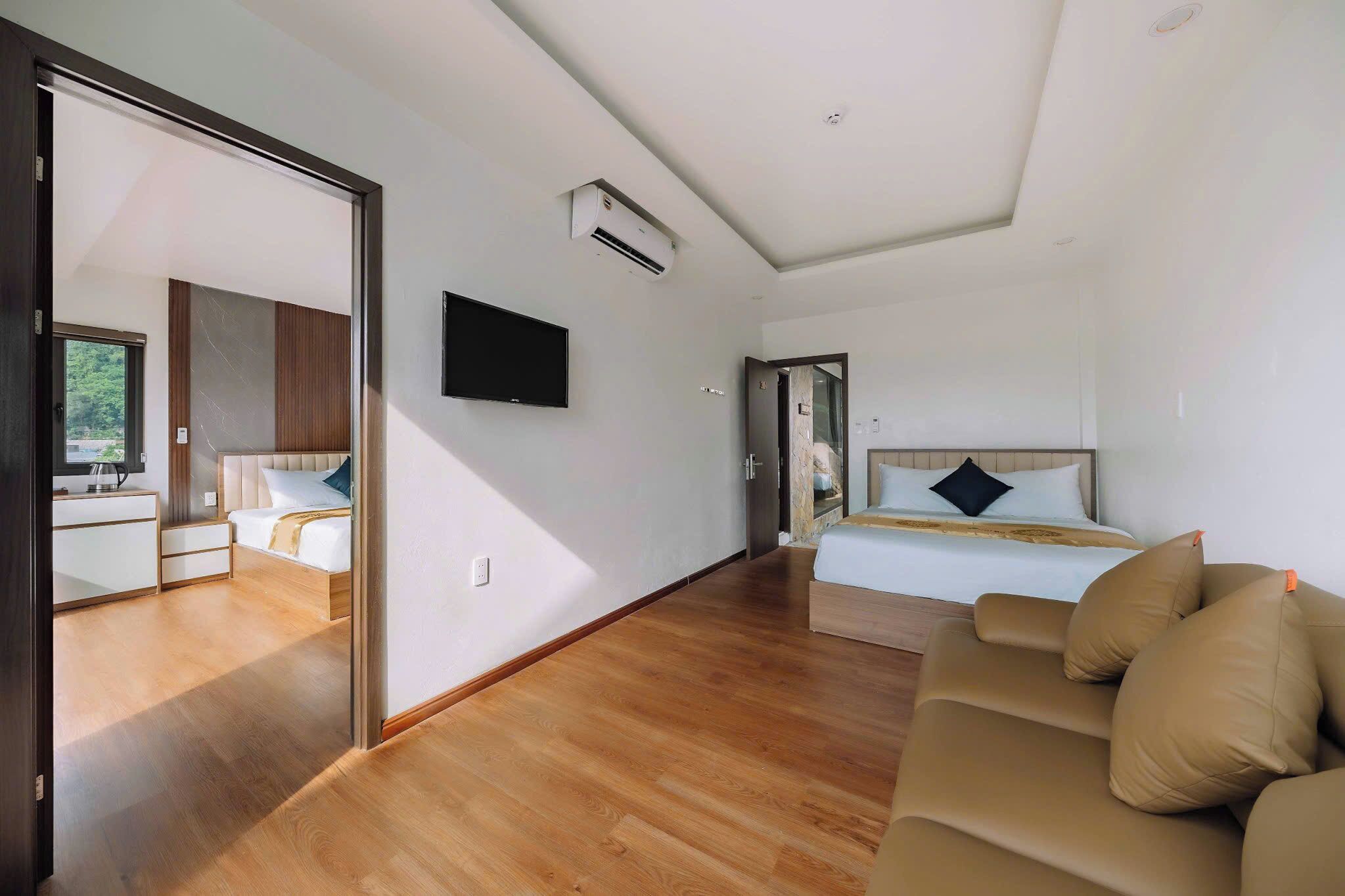 Quarto de hotel moderno com piso de madeira, um sofá, uma cama com cabeceira, uma televisão de tela plana e um ar condicionado.