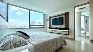 Quarto de hotel moderno com uma cama grande, televisão de tela plana na parede e vista para a cidade através de amplas janelas.
