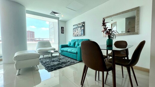 Uma sala de estar moderna com um sofá verde-água, uma poltrona branca e uma mesa de jantar de vidro com cadeiras marrons.