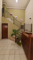 Uma escadaria com corrimão de madeira, um vaso de planta e quadros nas paredes.