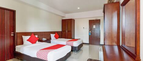Quarto de hotel com duas camas, um guarda-roupa de madeira, um banco e uma lixeira.