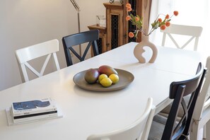 Uma mesa de jantar com uma travessa de frutas, um vaso de flores e um livro.