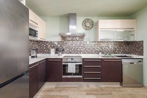 Uma cozinha moderna com geladeira de aço inoxidável, eletrodomésticos Bosch, painel de fundo estampado e lava-louças.