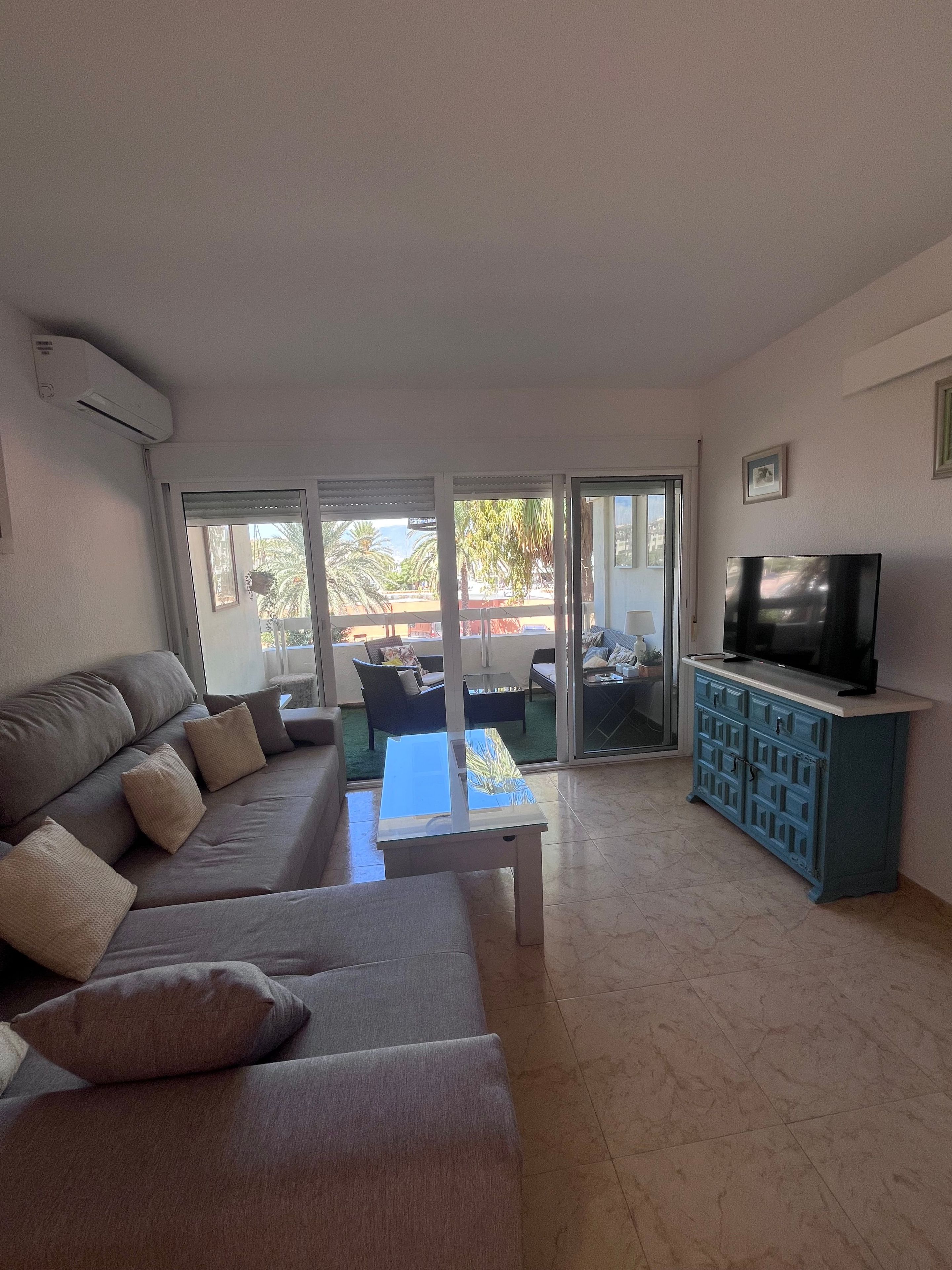 Sala de estar com sofá, mesa de centro, televisão e porta de vidro deslizante que dá para uma área externa.