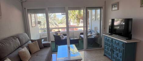 Sala de estar com sofá, mesa de centro, televisão e porta de vidro deslizante que dá para uma área externa.