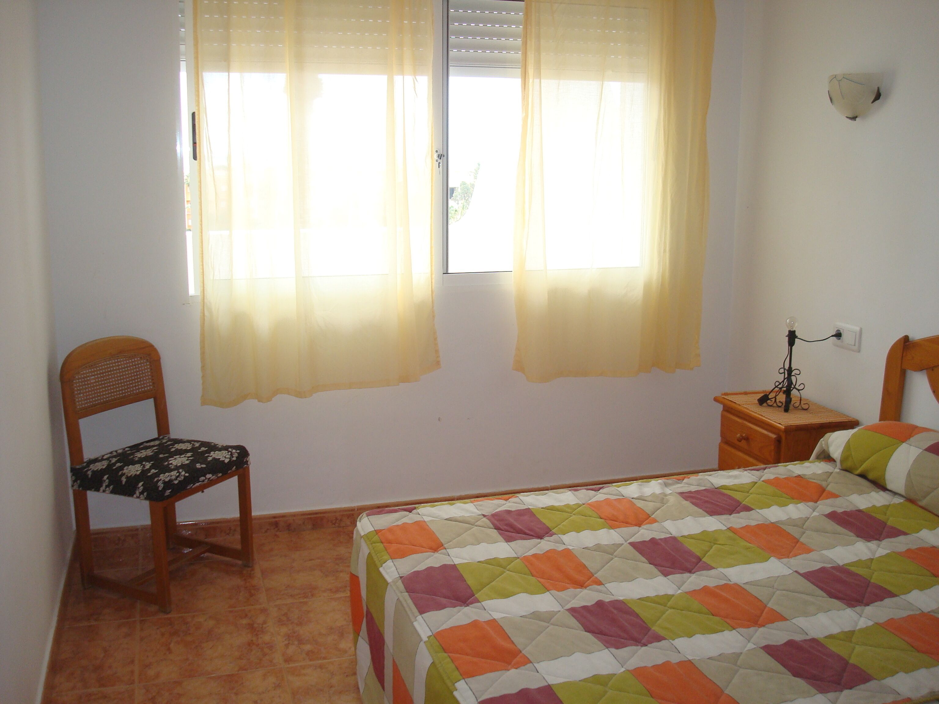 Quarto com cama, cadeira, mesa de cabeceira e janela com cortinas.