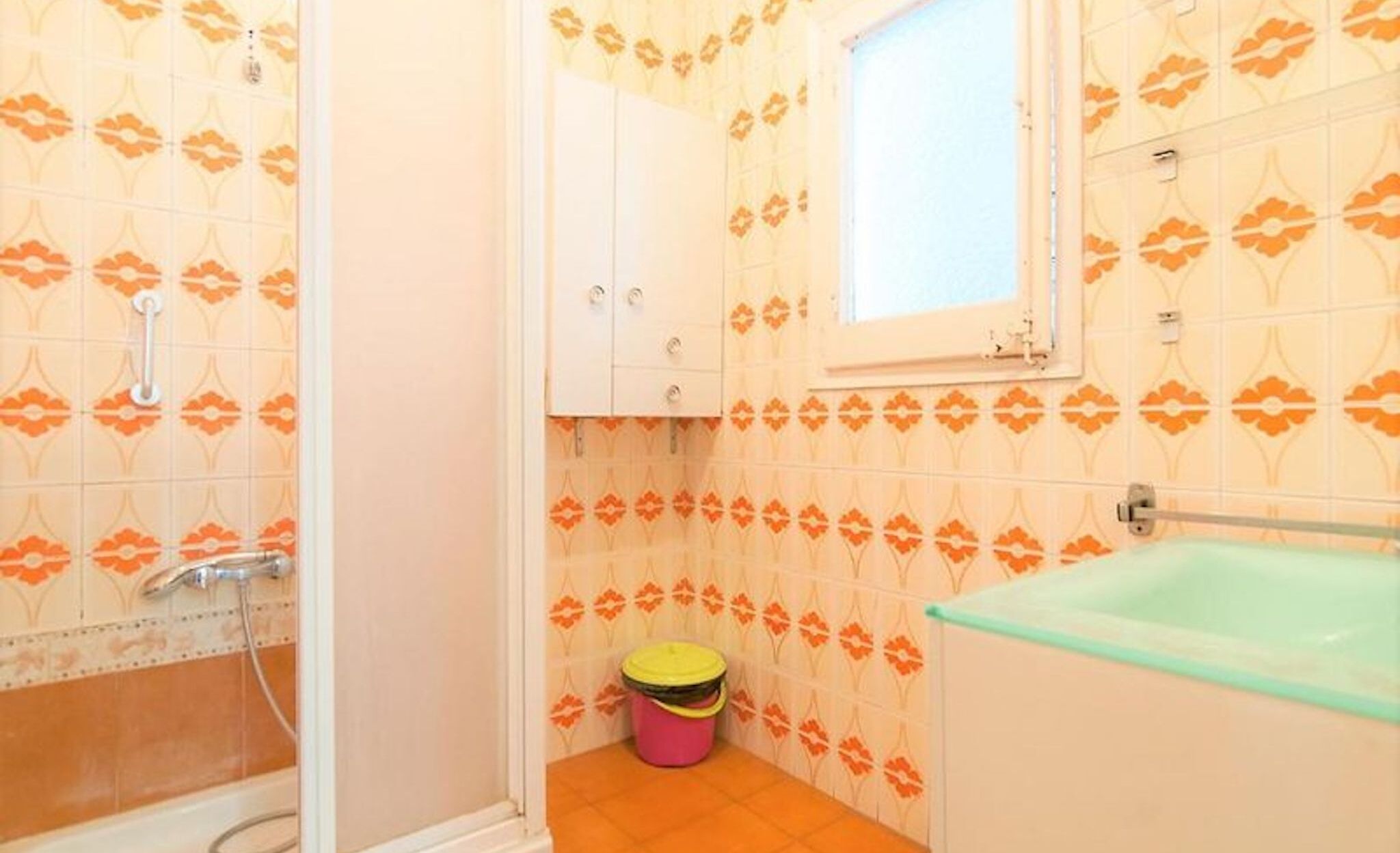 Casa de banho com azulejos estampados, chuveiro, pia e janela.