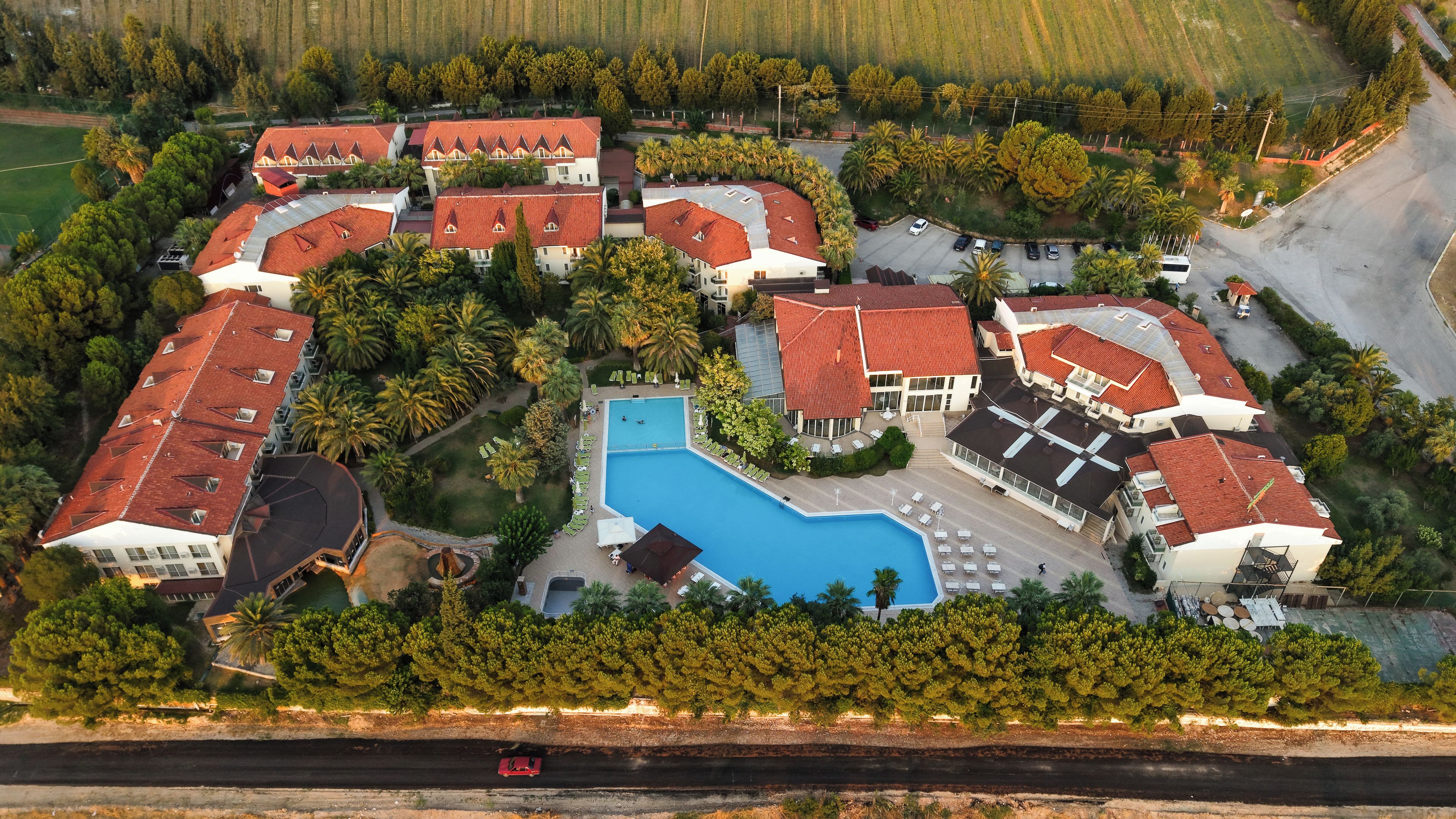 Vista aérea de um resort com vários edifícios, uma piscina e vegetação ao redor.