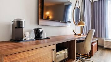 Quarto de hotel moderno com uma escrivaninha de madeira, uma cafeteira Keurig, micro-ondas, um espelho grande e uma luminária.
