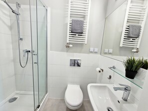 Casa de banho moderna com cabine de chuveiro em vidro, sanita branca, lavatório com prateleira de vidro e espelho sobre o lavatório.
