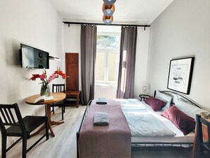 Quarto de hotel com cama, escrivaninha, cadeira, televisão e janela com cortinas.