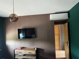 Quarto com televisão de tela plana fixada na parede, um armário de madeira abaixo e um aparelho de ar condicionado na parede.