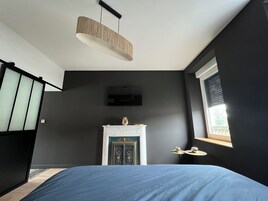 Quarto com cama, luminária pendente, lareira e janela com persianas.