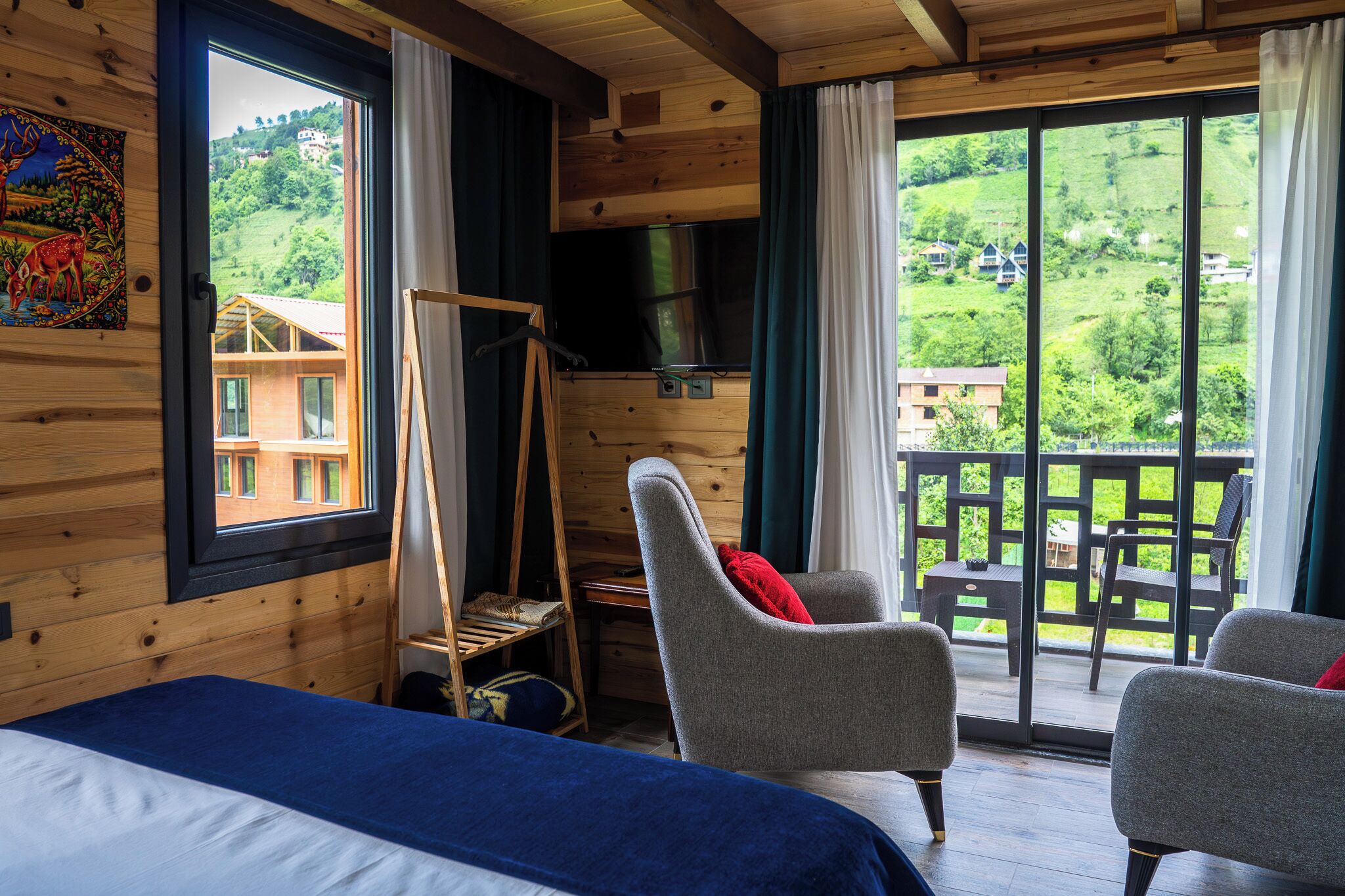 Quarto com cama, cadeira, televisão e vista para uma paisagem verde.