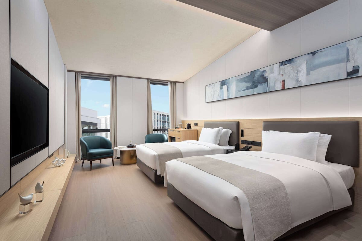 Quarto de hotel com duas camas, televisão, secretária e vista para a cidade.