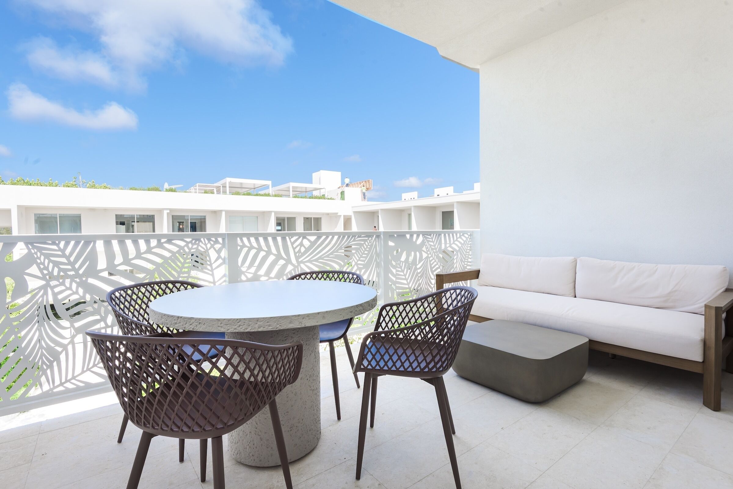 Varanda com mesa redonda e cadeiras, um sofá branco e vista para edifícios ao fundo.