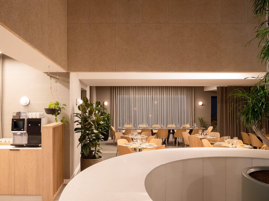 Um restaurante moderno com área de estar em curva, um canto para café e plantas em vasos.
