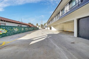 Uma garagem de estacionamento com um mural na parede esquerda, uma galeria coberta no lado direito e céu azul acima.