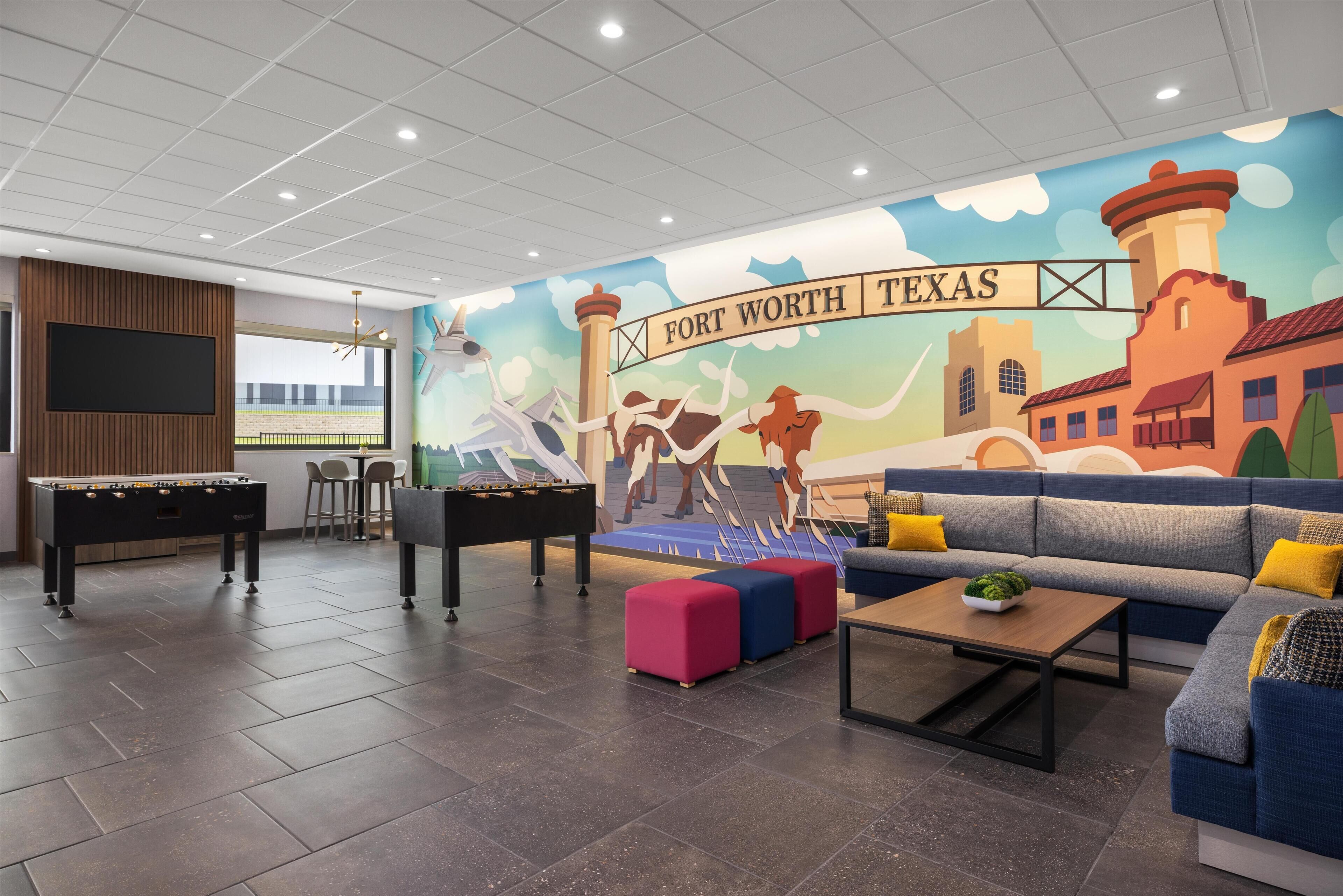 Um quarto com uma mesa de futebol de mesa, um sofá, pufes e um mural de Fort Worth, Texas.