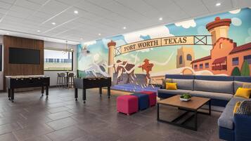 Um quarto com uma mesa de futebol de mesa, um sofá, pufes e um mural de Fort Worth, Texas.