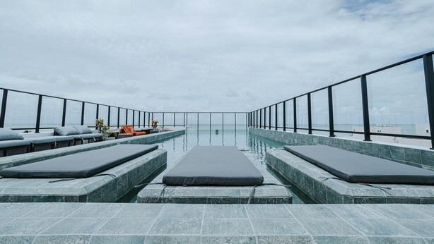 Piscina infinita no terraço, com espreguiçadeiras e barreira de vidro.