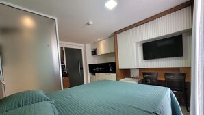 Quarto de hotel com cama, televisão, cozinha compacta e banheiro.