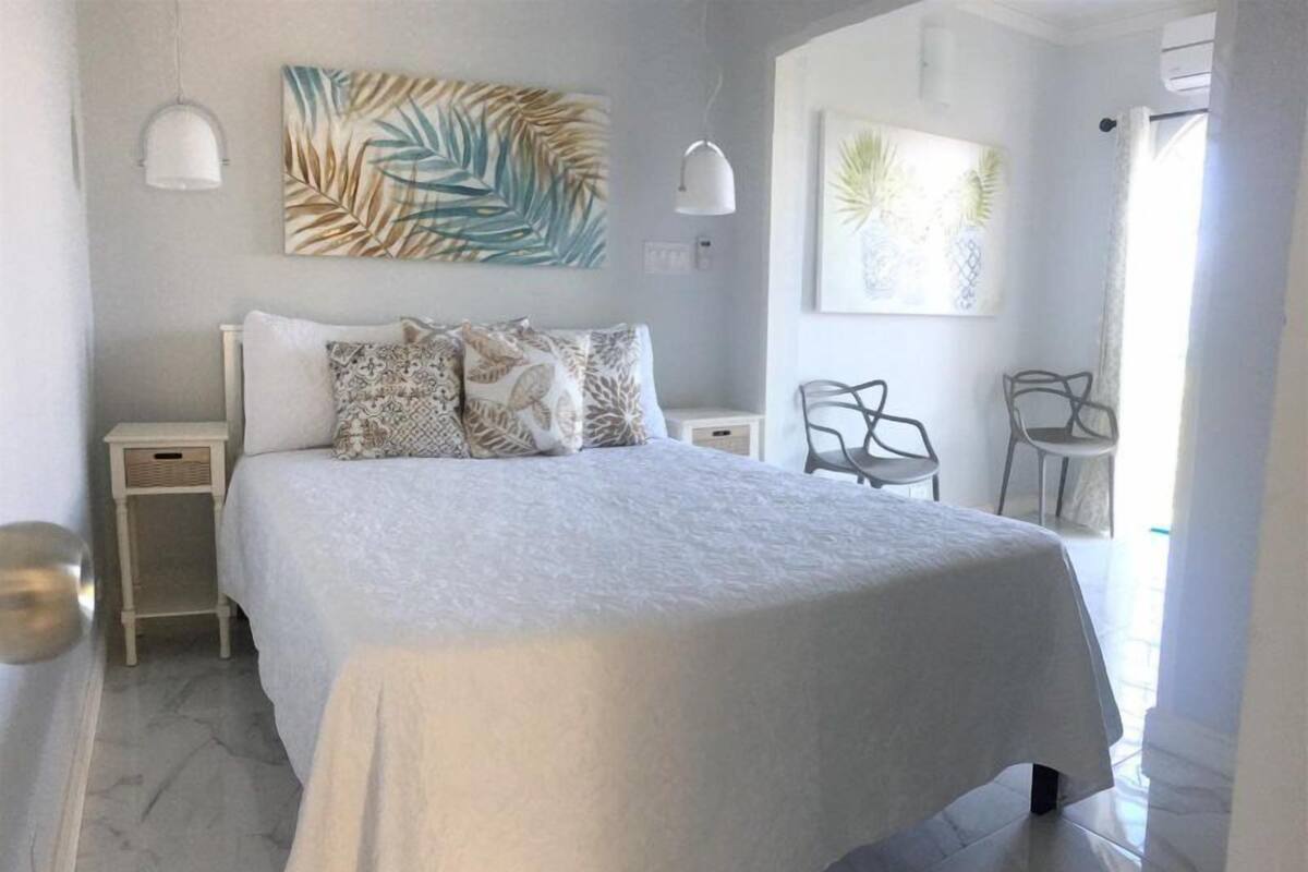 Quarto com cama grande, duas mesinhas de cabeceira, um criado-mudo e uma cadeira. Há duas luminárias de parede e duas obras de arte emolduradas acima da cama.