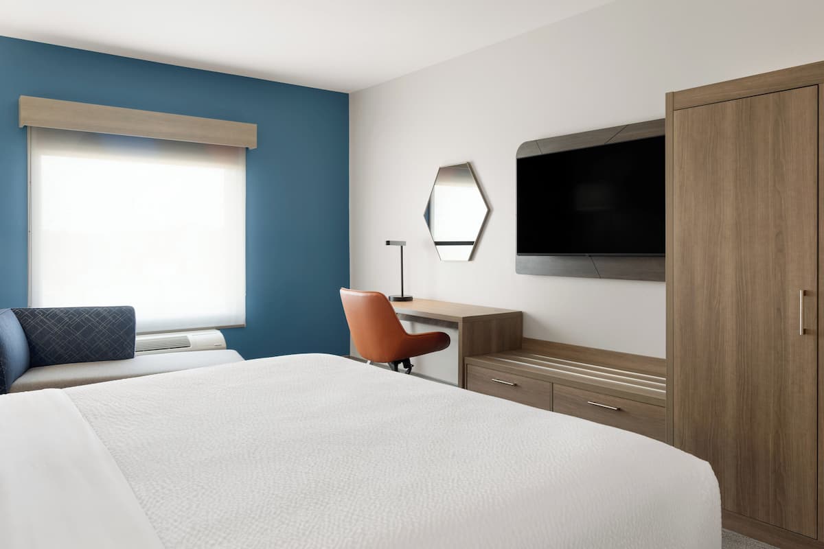 Quarto de hotel com uma cama grande, uma escrivaninha com cadeira, televisão e guarda-roupa.