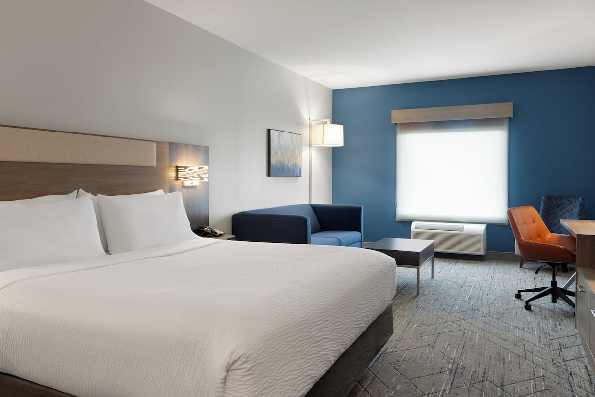 Quarto de hotel com uma cama grande, uma escrivaninha, uma cadeira e um sofá.