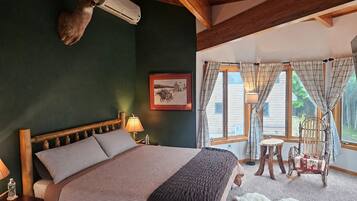 Quarto com cama, cabeça de veado montada, quadro emoldurado, cadeira e janela com cortinas.