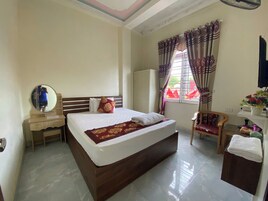 Quarto de hotel com uma cama grande, mesa de cabeceira de madeira, espelho, cadeira, escrivaninha e janela com cortinas.