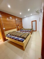 Quarto com duas camas de madeira, cabeceiras de madeira, uma pequena estante e uma porta.