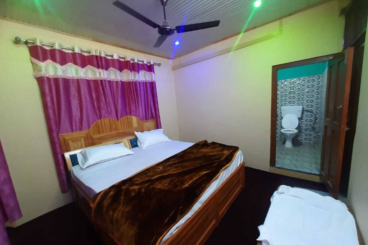 Quarto com cama de madeira, ventoinha no teto e banheiro com vaso sanitário e box.