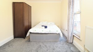 Quarto com uma cama de solteiro, um guarda-roupa e uma janela com cortinas.